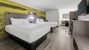 Quarto de hotel com duas camas, cabeceira de madeira, televisão de tela plana, escrivaninha com cadeira e banheiro visível através de uma porta aberta.