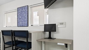 Espaço de trabalho com duas cadeiras, uma mesa, um monitor de computador e um aviso fixado na parede com a inscrição 'BUSINESS CENTER'.
