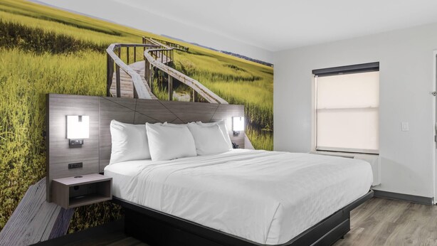 Quarto com cama, mesa de cabeceira, luminária na parede e janela.