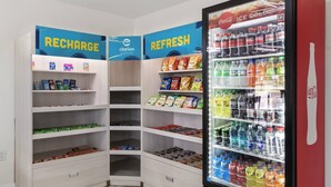 Canto de uma loja com prateleiras cheias de lanches, bebidas e um refrigerador.
