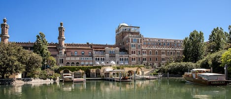 Um edifício histórico com uma torre imponente e uma cúpula, localizado às margens de um canal com barcos atracados.