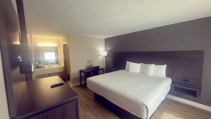 Quarto de hotel com uma cama grande, uma escrivaninha, uma cadeira, uma mesa de cabeceira, um abajur e um espelho.