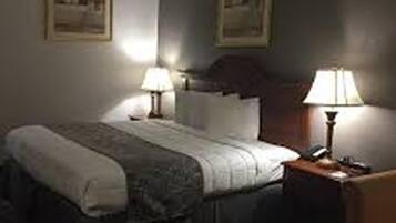 Quarto de hotel com uma cama, duas luminárias de cabeceira, uma cadeira e duas molduras na parede.