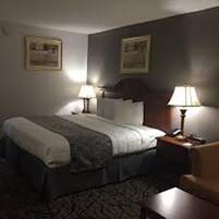 Quarto de hotel com uma cama, duas luminárias de cabeceira, uma cadeira e duas molduras na parede.