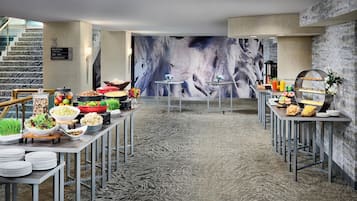 Um quarto amplo com escadaria de mármore, um grande mural na parede e uma mesa de buffet com diversos alimentos e bebidas.