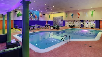 Piscina interior com piso xadrez, cadeiras à beira da piscina e uma tela de projeção exibindo personagens animados.