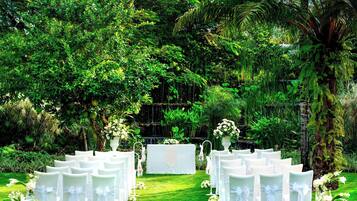 Local de casamento ao ar livre com fileiras de cadeiras brancas e um altar branco.