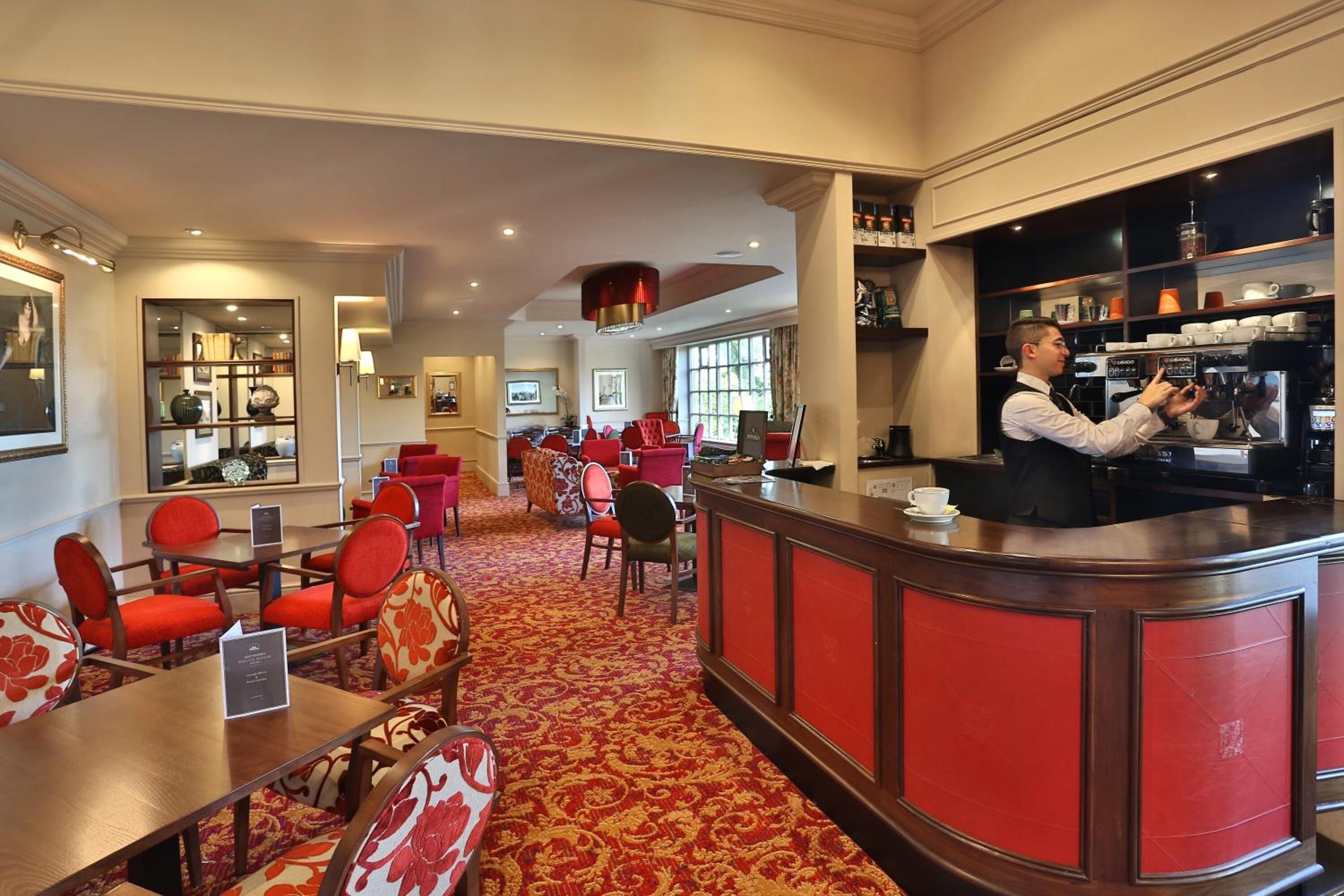 Um hall de hotel com carpete vermelho, balcão de recepção e área de bar.