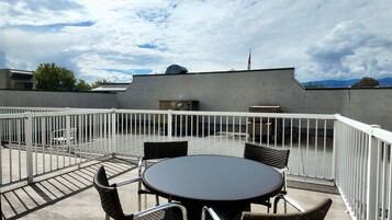 Terraço no telhado com uma mesa redonda e cadeiras, ladeado por um guarda-corpo de metal branco.