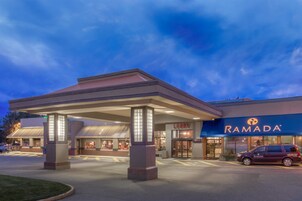 Entrada do hotel Ramada com área de estacionamento coberta e saguão visível.