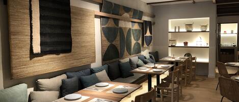 Um restaurante moderno com mesas comunitárias grandes, assentos acolchoados e arte decorativa nas paredes.