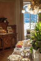 Mesa de buffet com diversos alimentos e vista para um corpo de água através de uma janela.