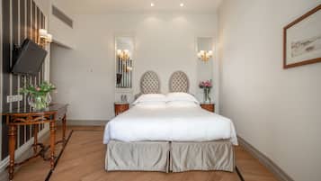Quarto bem arrumado com cama grande, mesa de cabeceira com um vaso e televisão de tela plana na parede.