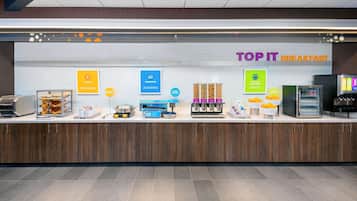 Espaço de café da manhã com uma placa indicando "TOP IT BREAKFAST" e diversas opções de comida à mostra.