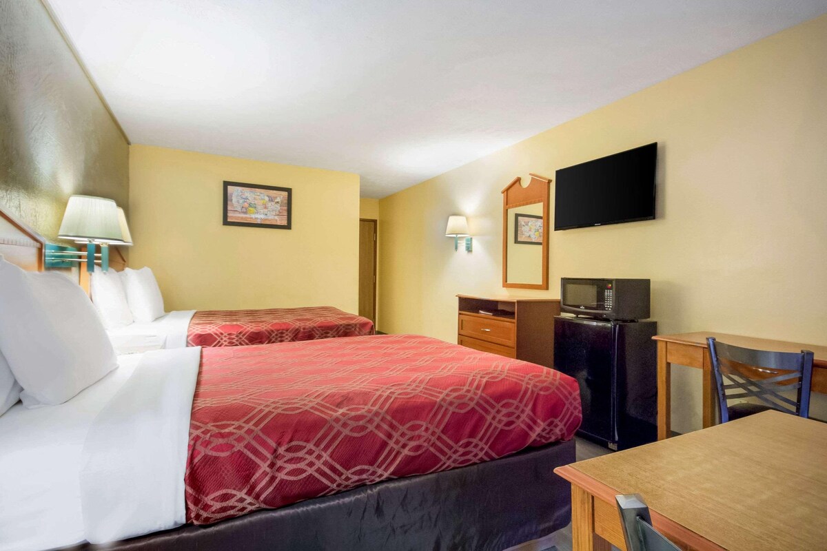Quarto de hotel com duas camas, uma escrivaninha, televisão, micro-ondas e uma cadeira.
