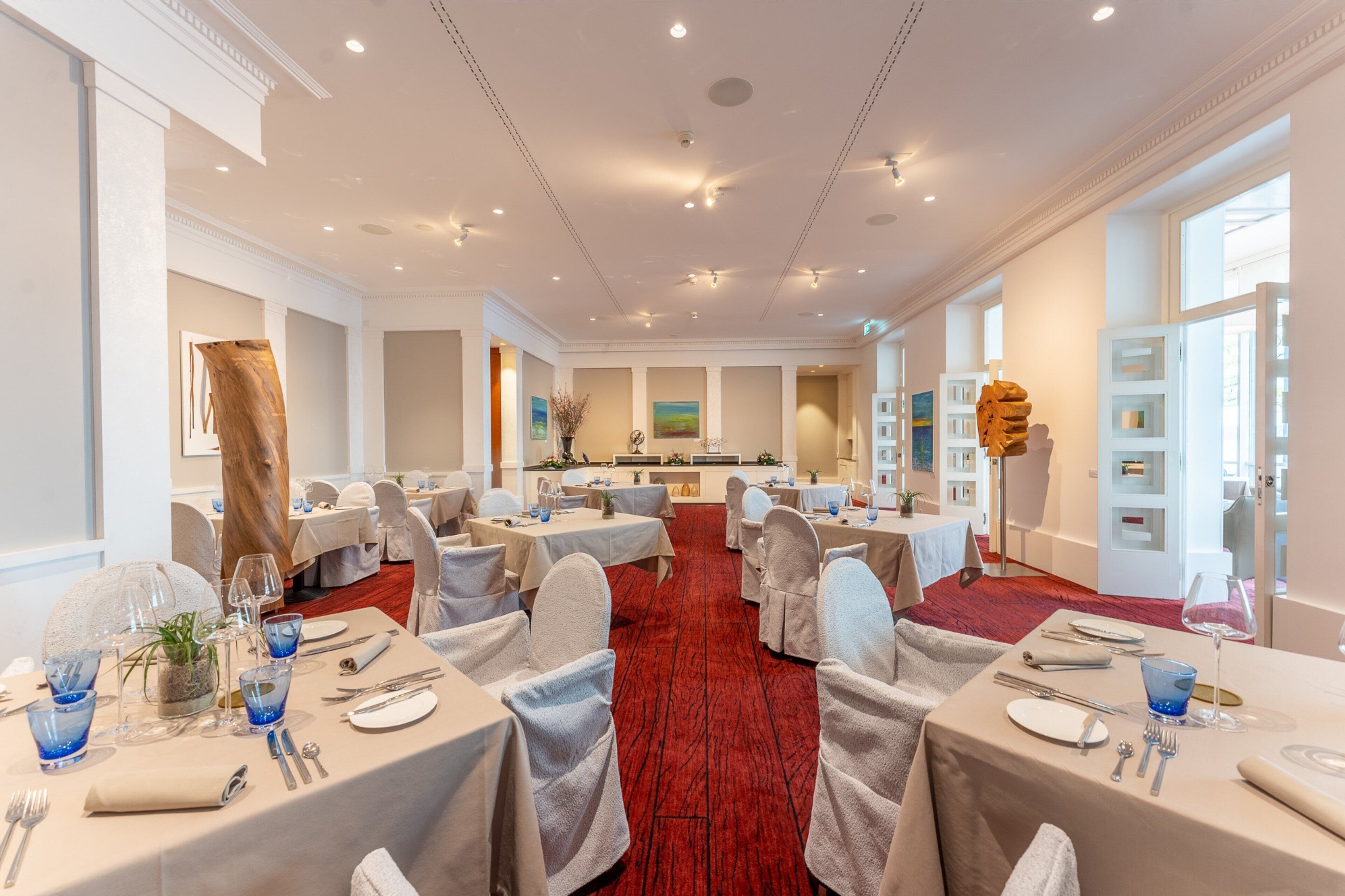 Uma sala de banquetes com mesas redondas, cadeiras brancas e carpete vermelho.