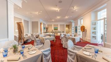 Uma sala de banquetes com mesas redondas, cadeiras brancas e carpete vermelho.