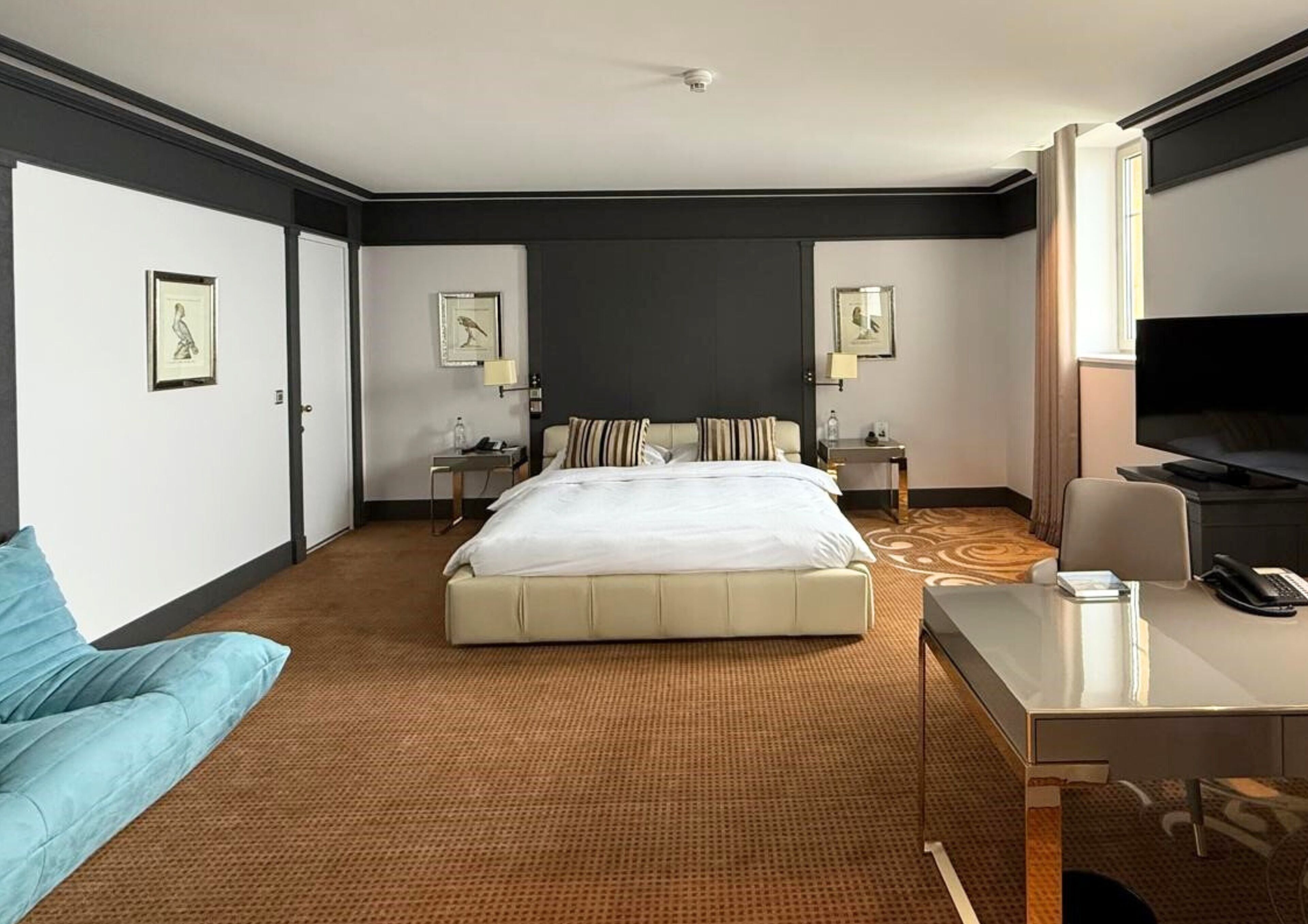Quarto de hotel com uma cama grande, uma escrivaninha, uma cadeira, uma televisão e duas mesas de cabeceira com abajures.