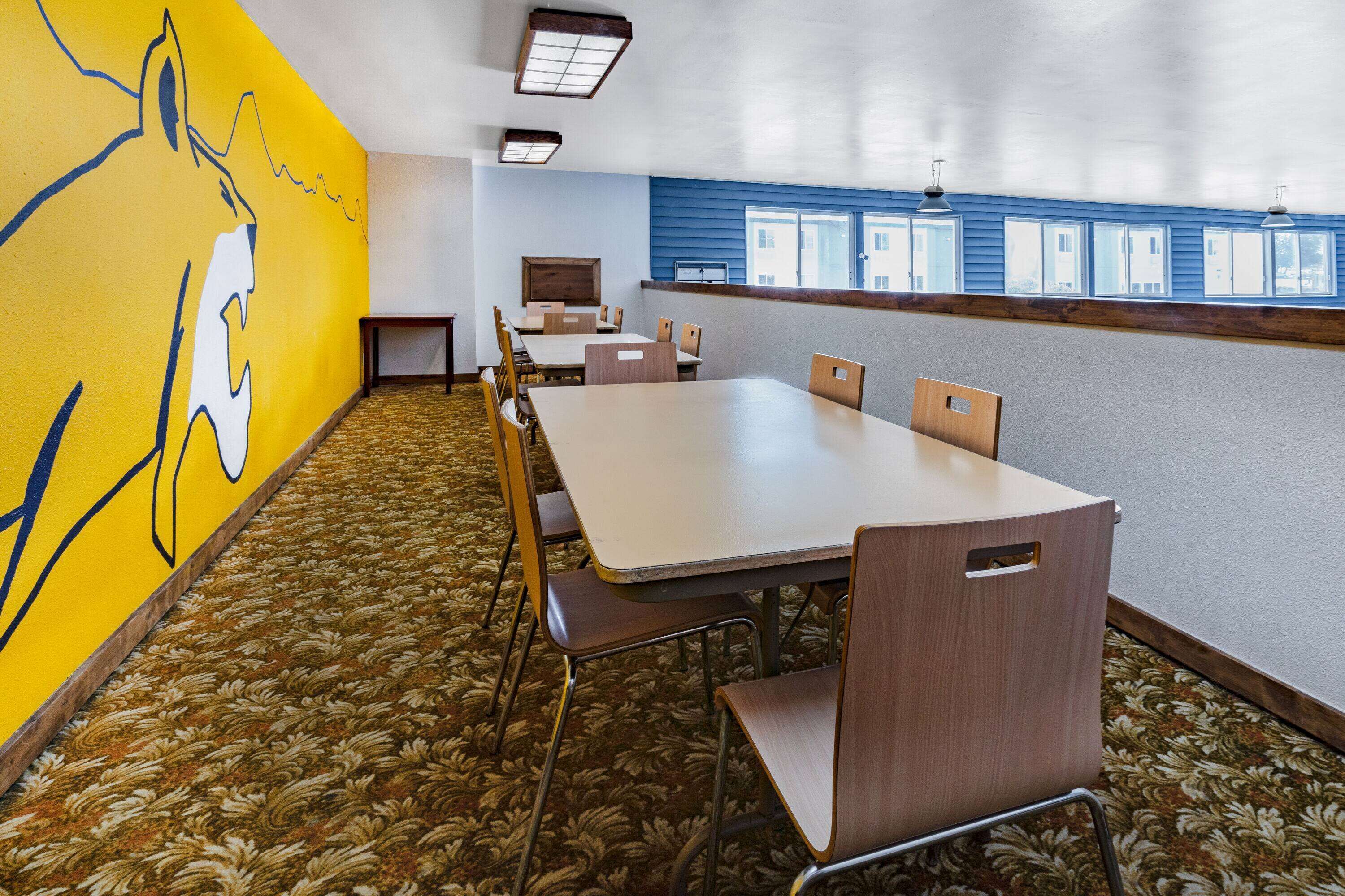 Uma sala de conferências com uma mesa grande, cadeiras, piso coberto por carpete e um mural na parede.