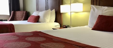 Quarto de hotel com duas camas, uma mesa de cabeceira, um abajur e uma cadeira.