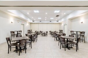 Uma sala de conferências com várias mesas e cadeiras, luminárias embutidas no teto e paredes brancas.