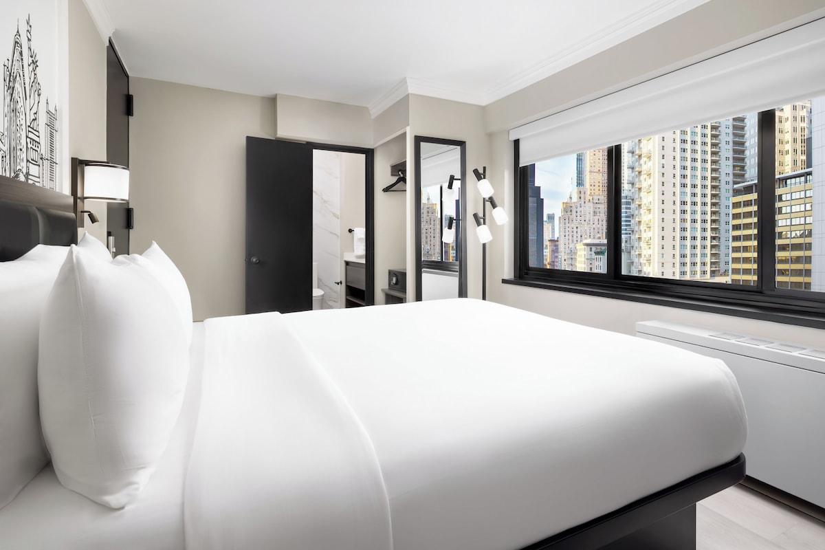 Quarto de hotel moderno com uma cama grande, banheiro e vista para a cidade.