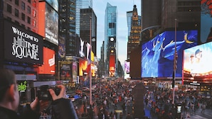 Cena de rua urbana movimentada, com edifícios altos e grandes outdoors.
