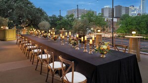 Uma área de refeições ao ar livre com uma mesa comprida, cadeiras, velas e flores.