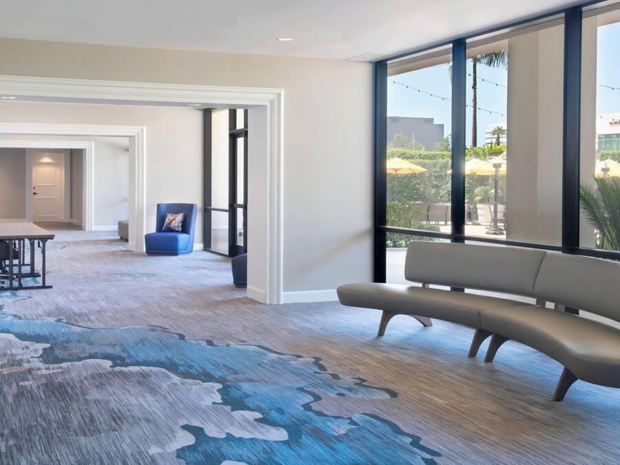 Quarto de hotel moderno com uma janela grande, um sofá, uma mesa de jantar e uma poltrona azul.