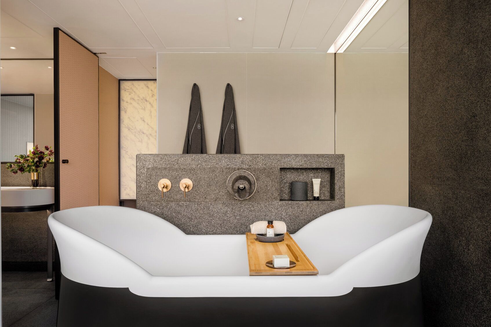 Um spa moderno com uma banheira grande e independente, um tabuleiro de madeira com produtos de higiene e uma prateleira com produtos para a pele.