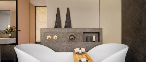 Um spa moderno com uma banheira grande e independente, um tabuleiro de madeira com produtos de higiene e uma prateleira com produtos para a pele.