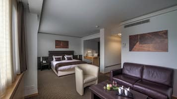 Quarto de hotel com cama, escrivaninha, sofá de couro e mesa de centro com bandeja de xícaras e flores.