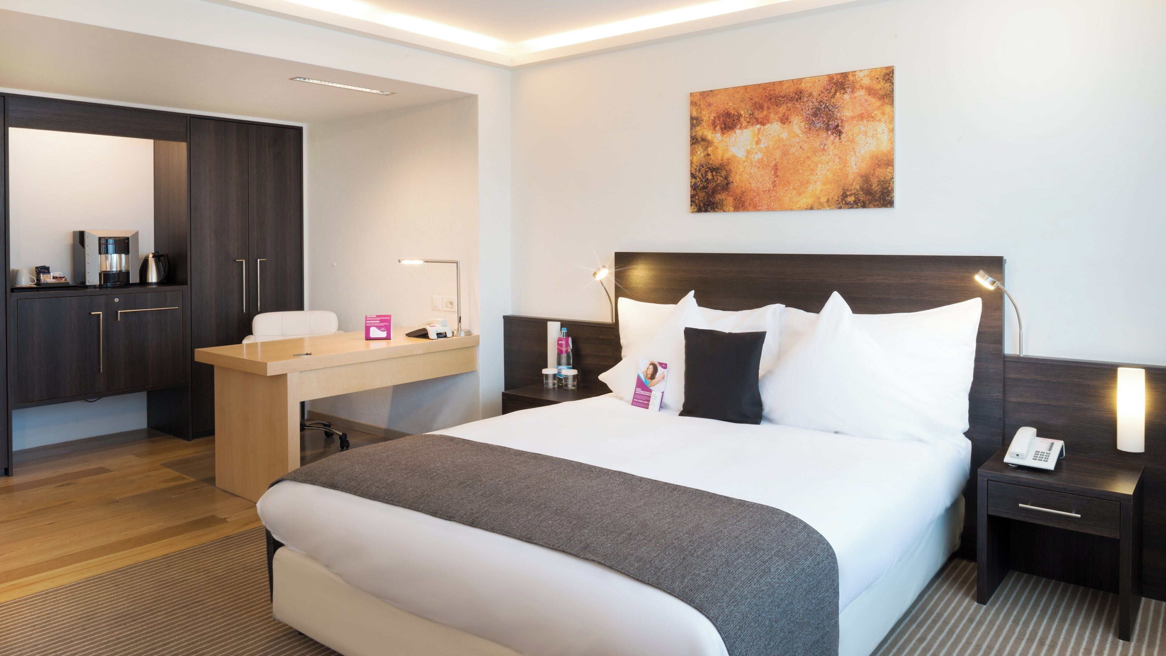 Quarto de hotel com cama, mesas de cabeceira, escrivaninha e espelho.