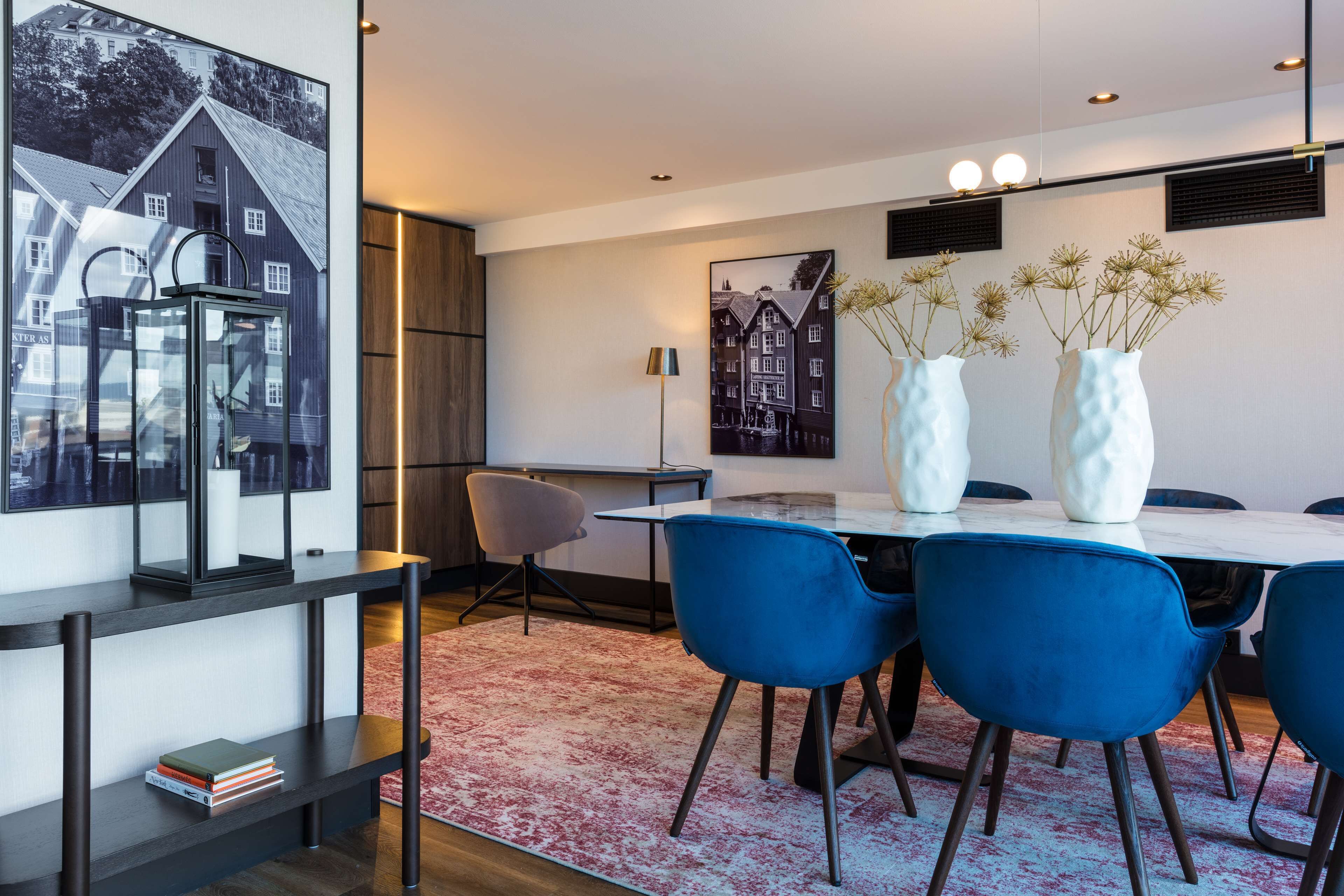 Uma sala de jantar moderna com uma mesa branca, cadeiras azuis e um tapete com padrão vermelho e branco.