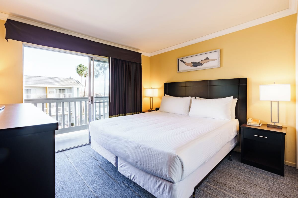 Quarto de hotel com uma cama grande, uma escrivaninha, uma mesa de cabeceira e vista para o exterior.