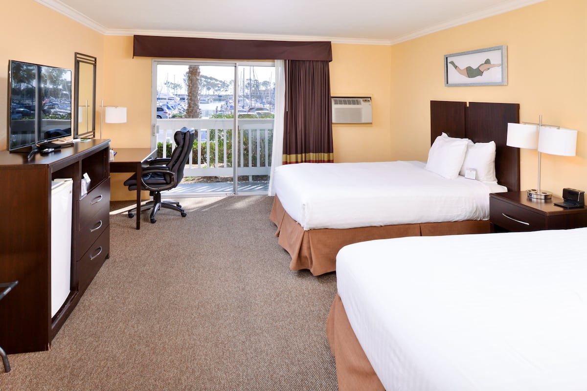 Quarto de hotel com cama, escrivaninha, cadeira, televisão e varanda com vista para a marina.