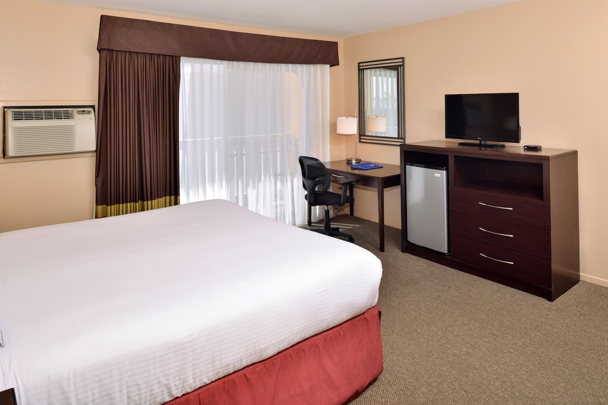 Quarto de hotel com cama, escrivaninha, televisão e frigorífico.