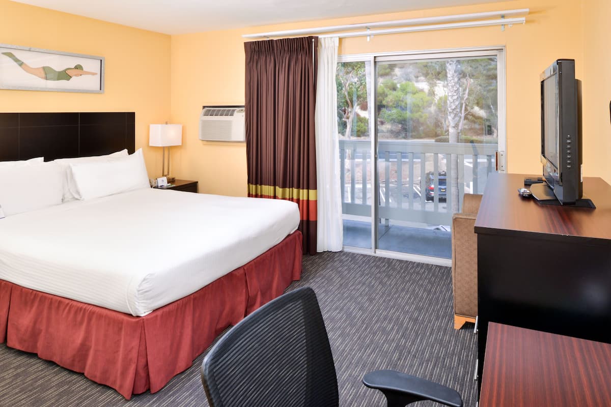 Quarto de hotel com uma cama grande, uma escrivaninha, uma cadeira, uma televisão e vista para a varanda.