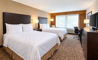 Quarto de hotel com duas camas, uma escrivaninha, televisão e janela com cortinas.