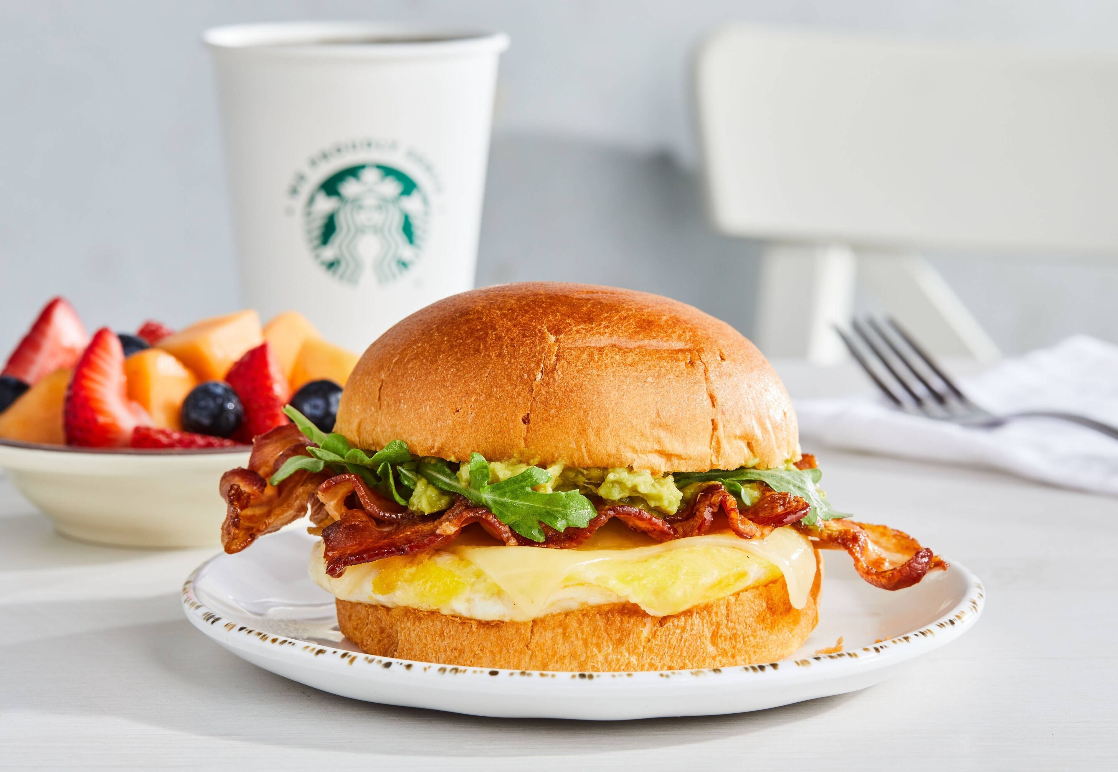 Um sanduíche de café da manhã em um prato, com uma xícara Starbucks ao fundo.