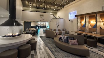 Uma área de lounge moderna com lareira central, assentos confortáveis e tela de projeção na parede.