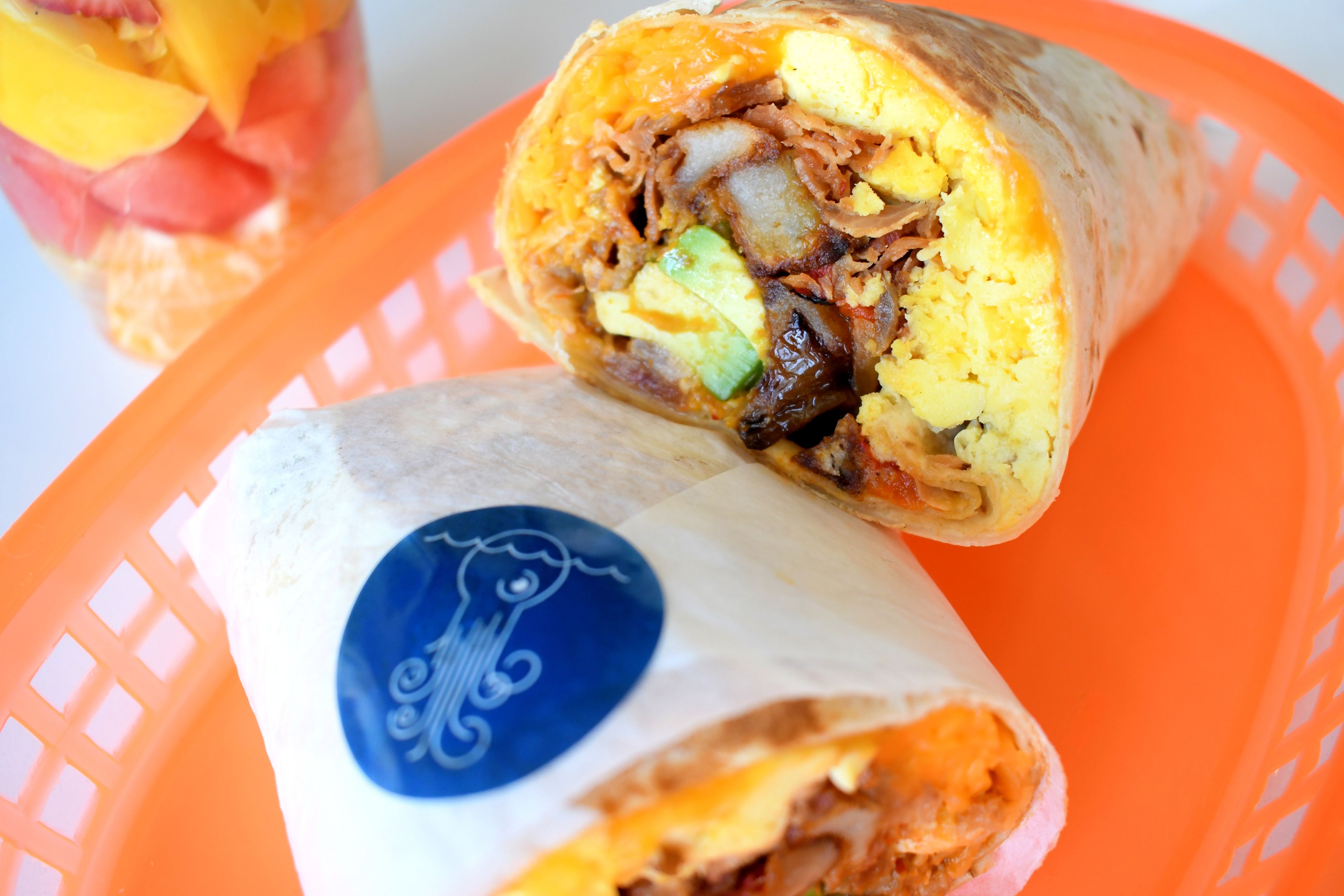 Burrito com recheio visível de carne, abacate e ovos, servido em um prato laranja.