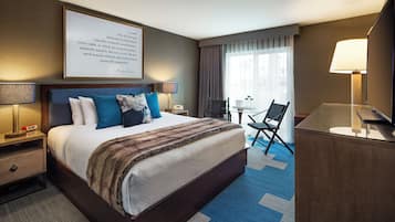 Quarto de hotel com cama grande, mesas de cabeceira, escrivaninha, cadeira e janela com cortinas.