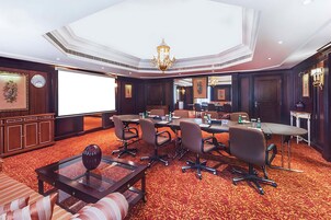 Sala de conferências com uma tela grande, várias mesas e cadeiras.