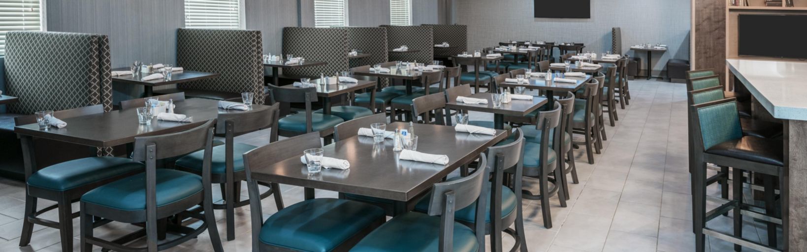 Um restaurante com várias mesas e cabines, cada uma com louça posta e cadeiras.