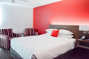 Quarto de hotel com uma cama grande, uma mesa de cabeceira com telefone e duas poltronas listradas.