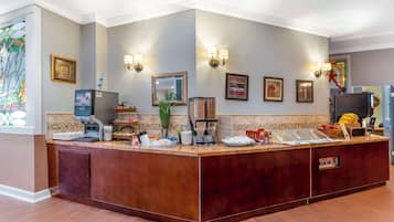 Uma área de recepção de hotel com um balcão marrom, luminárias fixadas na parede, obras de arte emolduradas e um espaço para café.