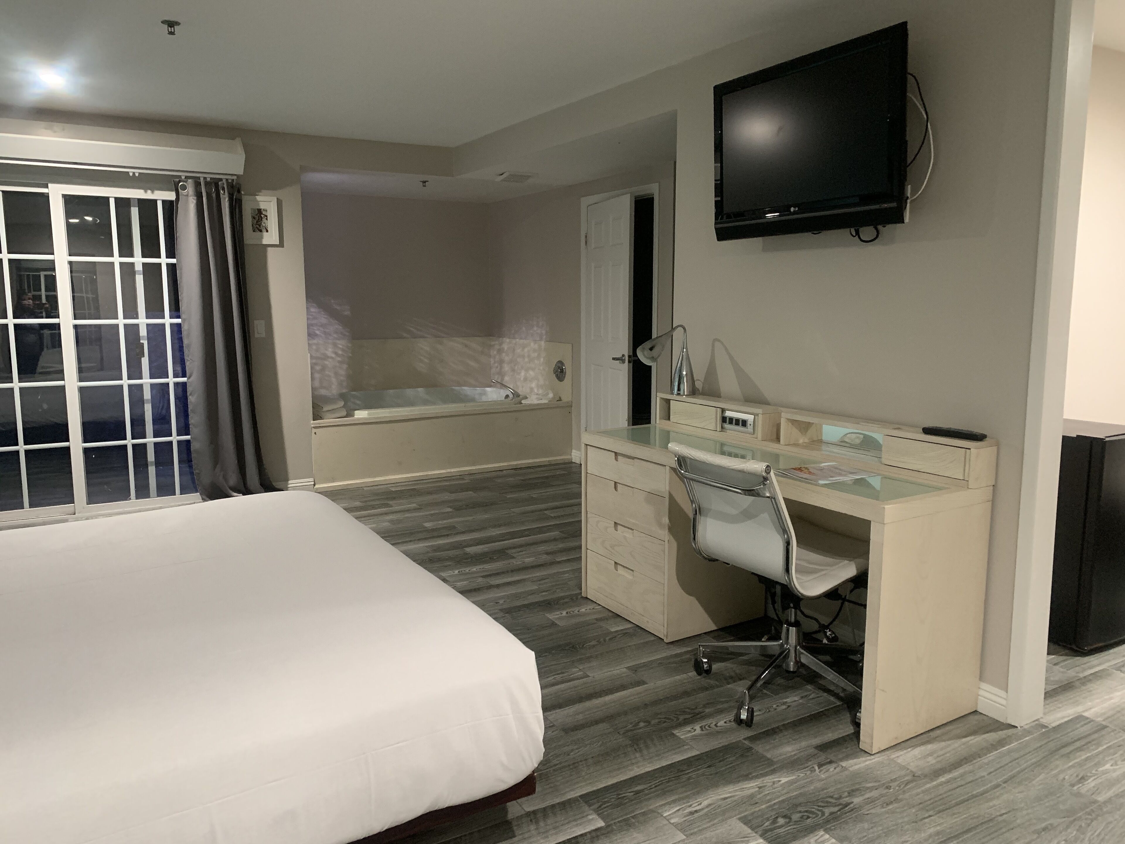 Quarto de hotel com cama, escrivaninha, cadeira, televisão e banheira.