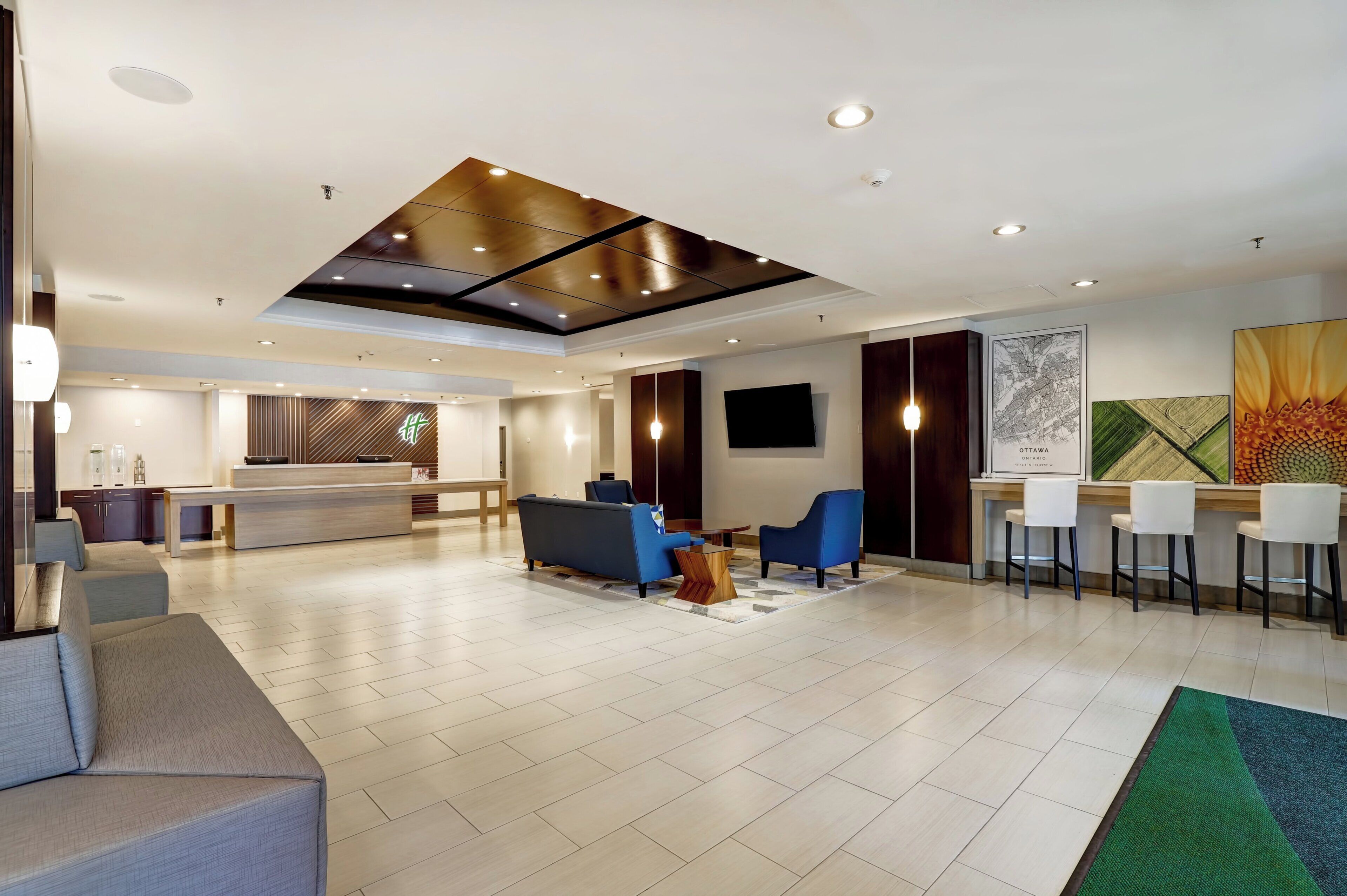 Um saguão de hotel moderno com balcão de recepção, área de estar e uma grande TV de tela plana.