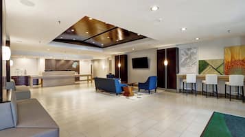 Um saguão de hotel moderno com balcão de recepção, área de estar e uma grande TV de tela plana.